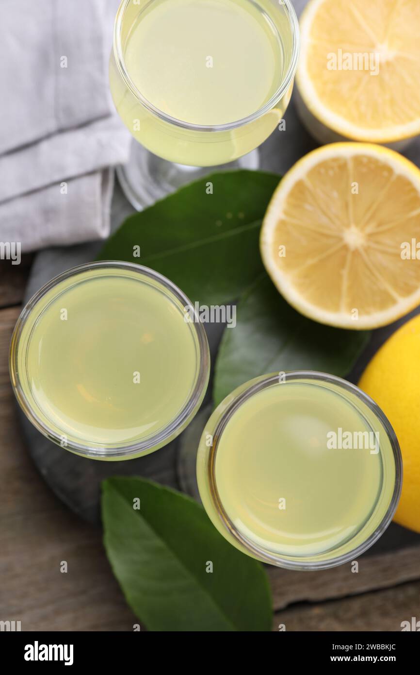Tasty limoncello liqueur, lemons and green leaves on table, top view ...