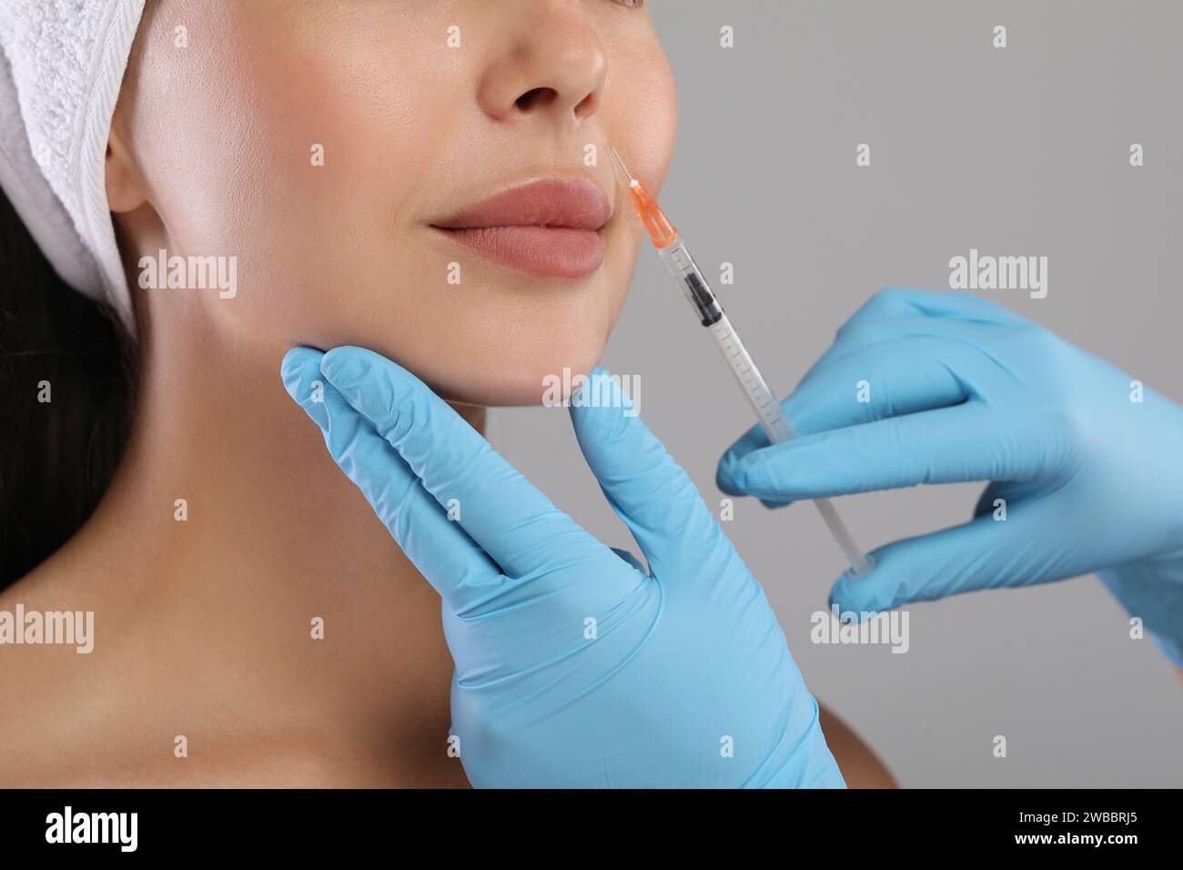 Doctor giving facial injection to young woman on light grey background ...