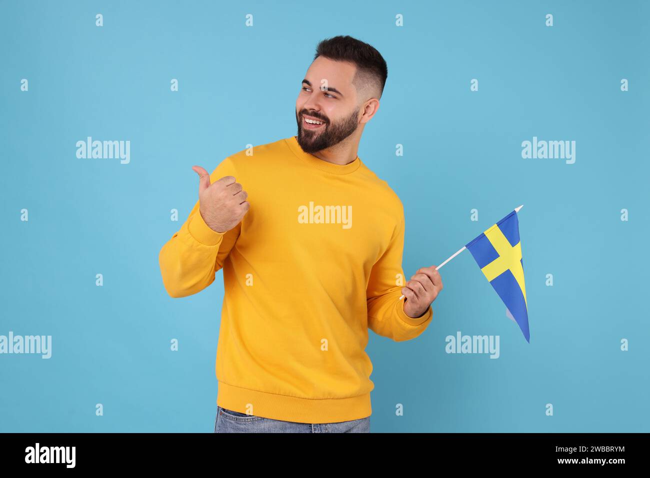 Young man holding flag of Sweden on light blue background Stock Photo ...