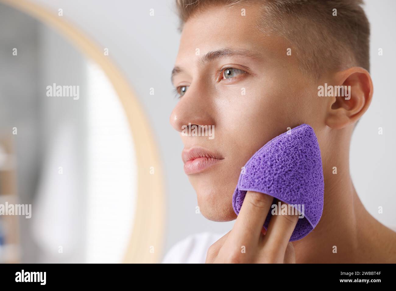 Young man washing his face with sponge in bathroom. Space for text ...