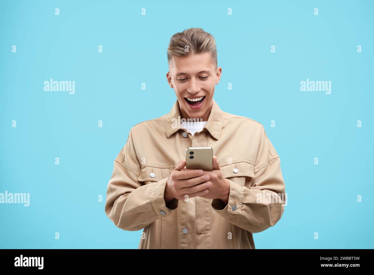 Emotional young man sending message via smartphone on light blue ...