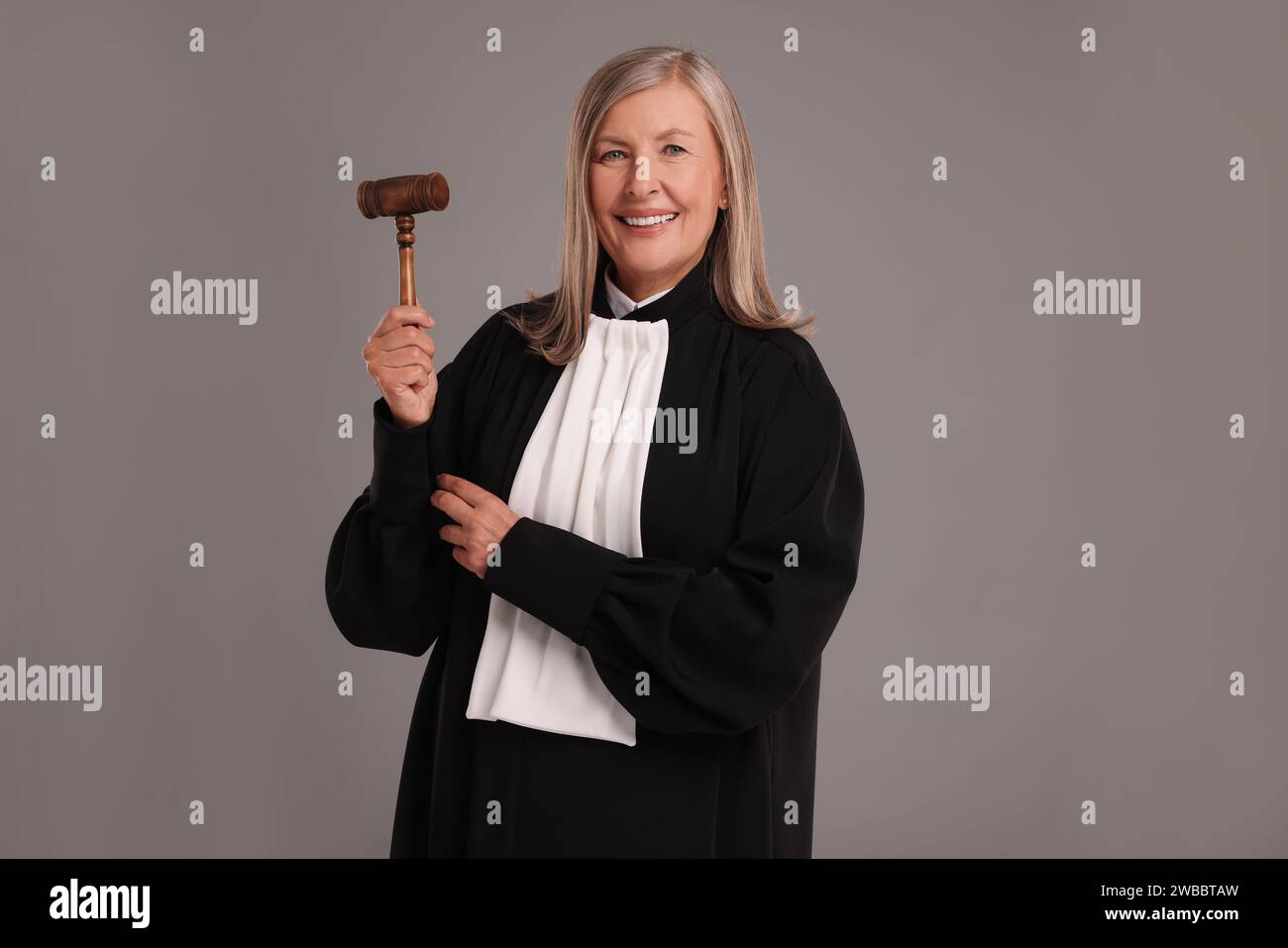 Smiling senior judge with gavel on grey background Stock Photo - Alamy