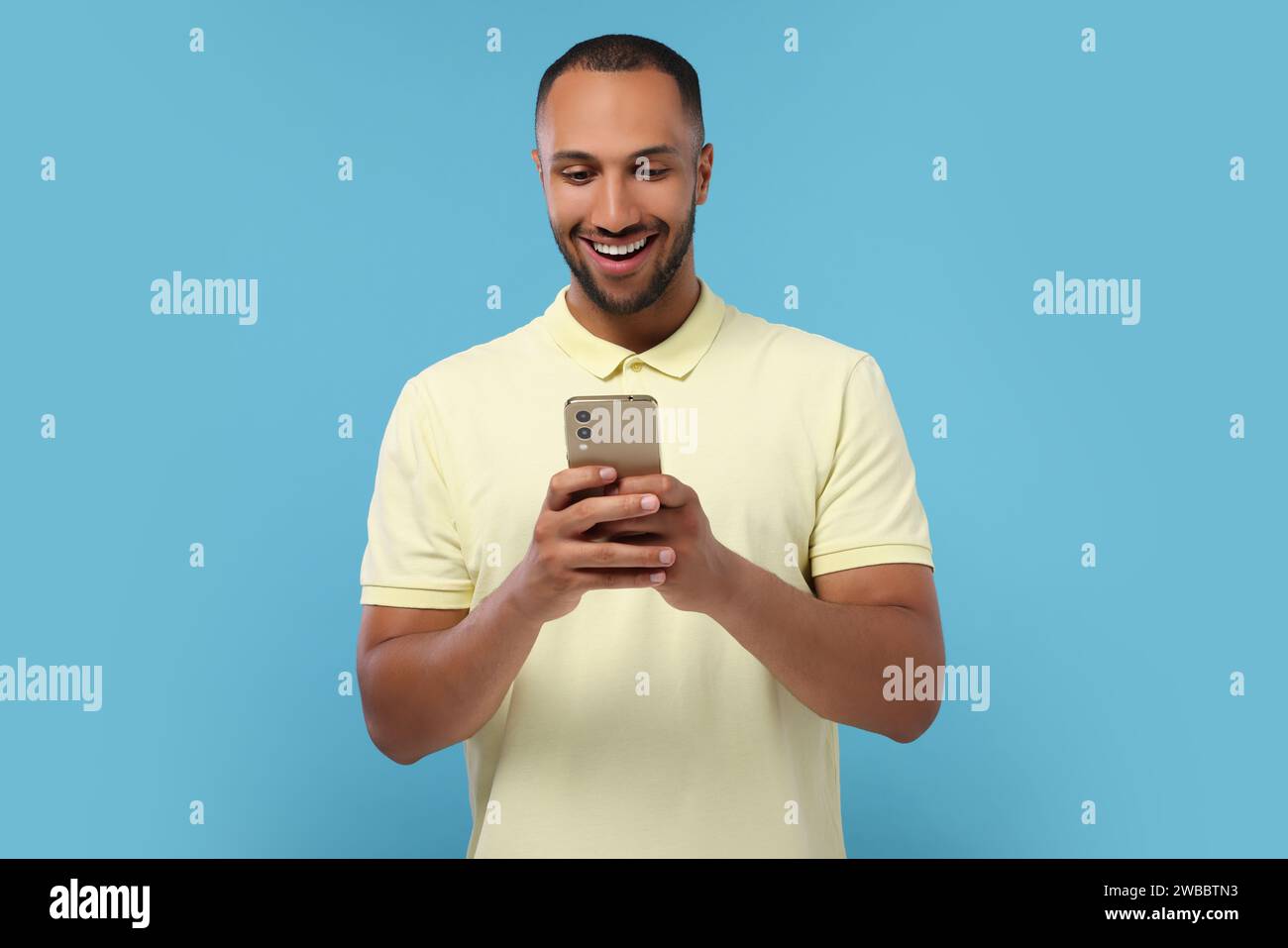 Happy man sending message via smartphone on light blue background Stock ...