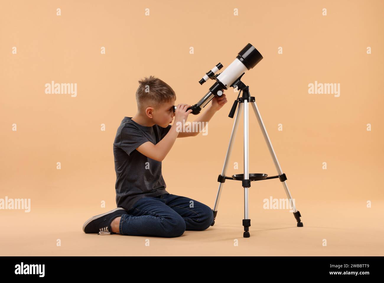 Little boy looking at stars through telescope on beige background Stock ...