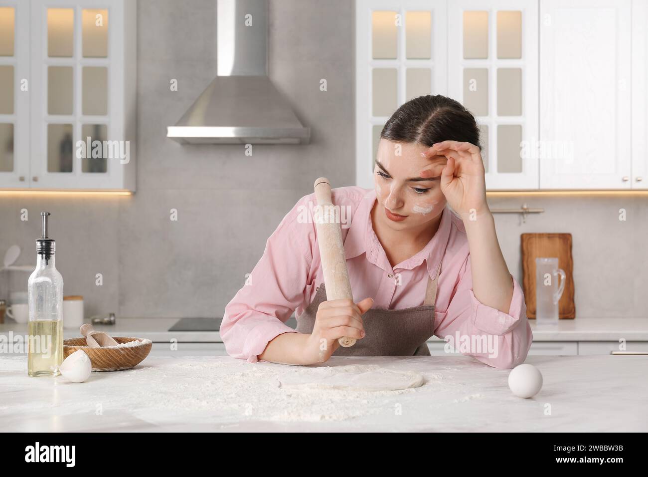Tired woman with soiled face holding rolling pin in messy kitchen Stock ...