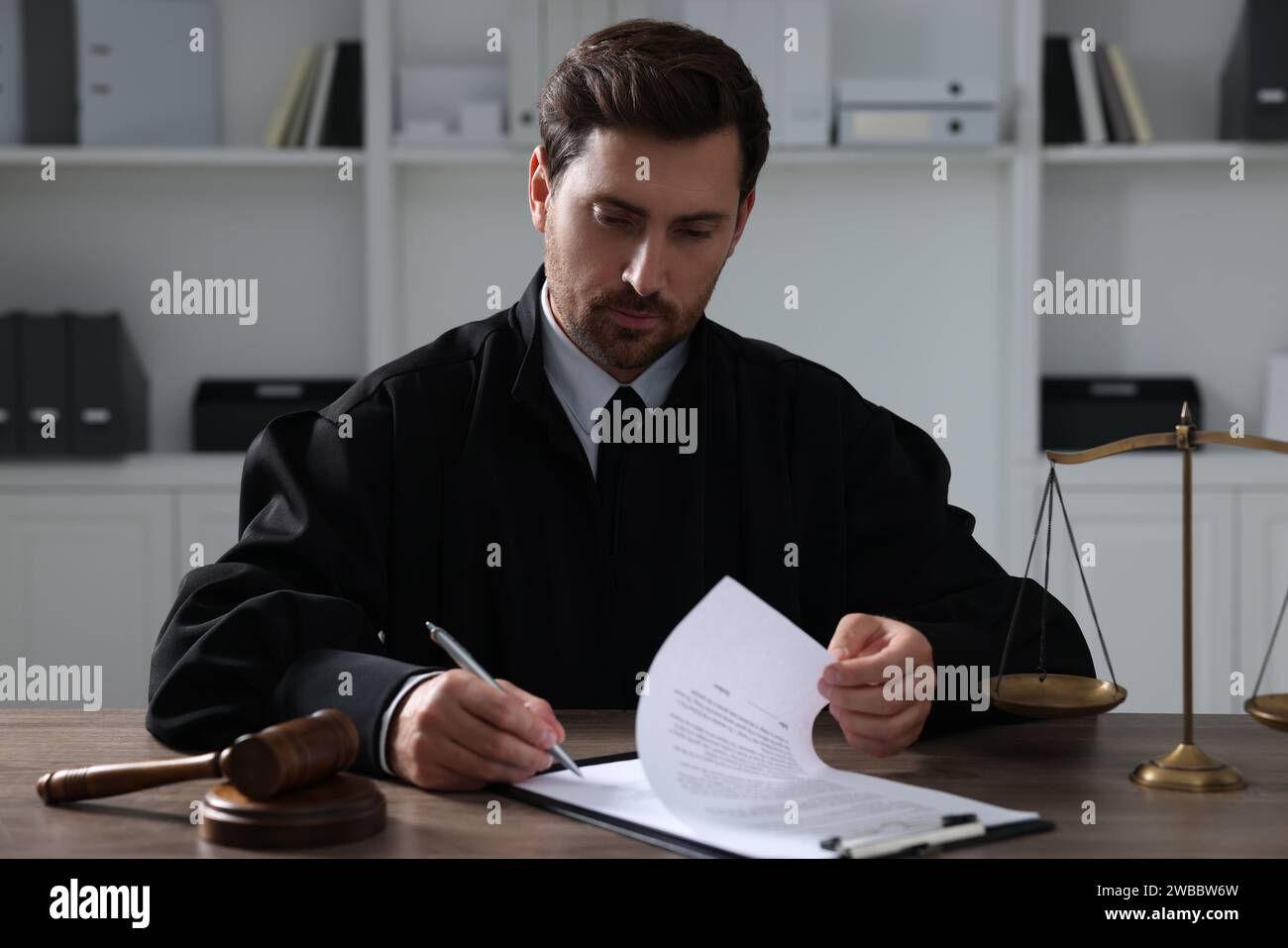 Judge with gavel writing in papers at wooden table in office Stock ...