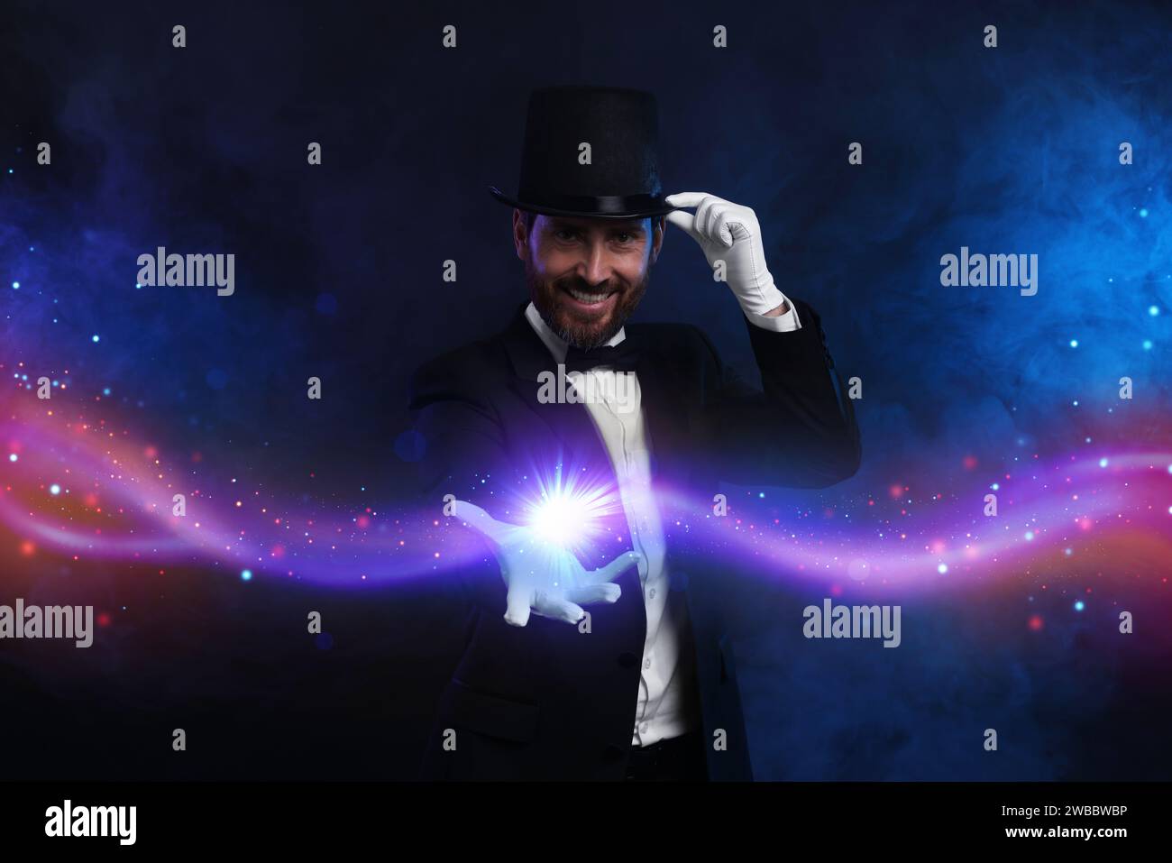 Smiling magician showing trick on dark background Stock Photo - Alamy