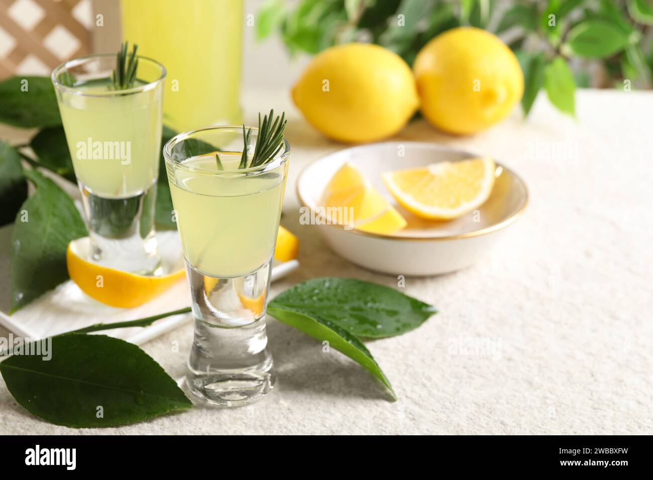 Tasty limoncello liqueur, lemons and green leaves on white textured ...