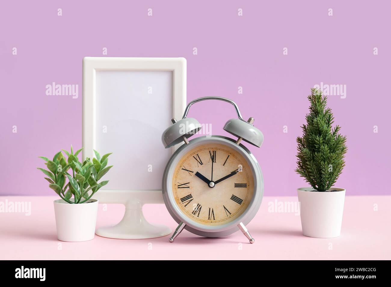 Artificial plants with alarm clock and blank frame on table near lilac ...