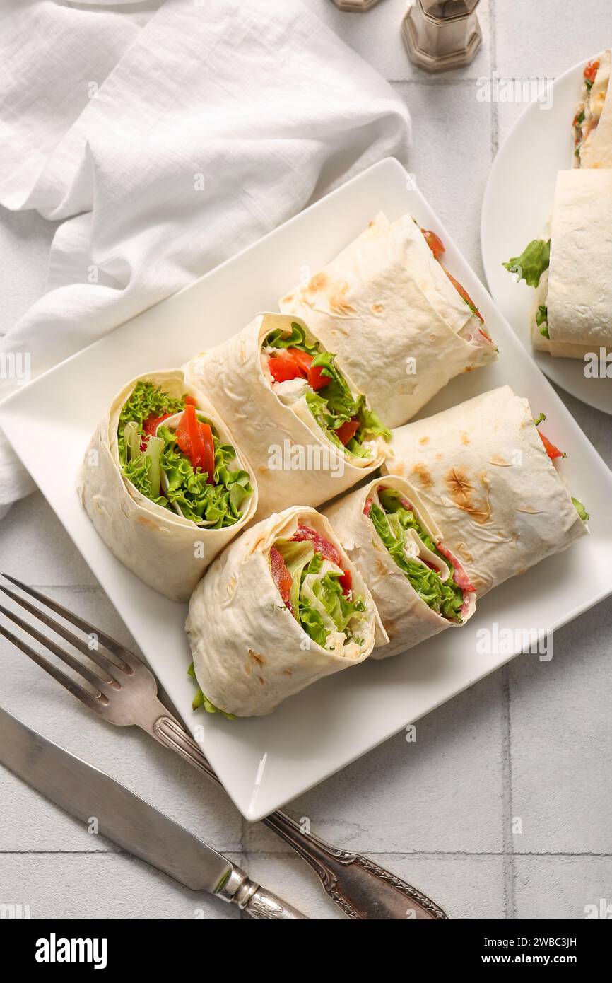 Plate of tasty lavash rolls with tomatoes and greens on white tile ...