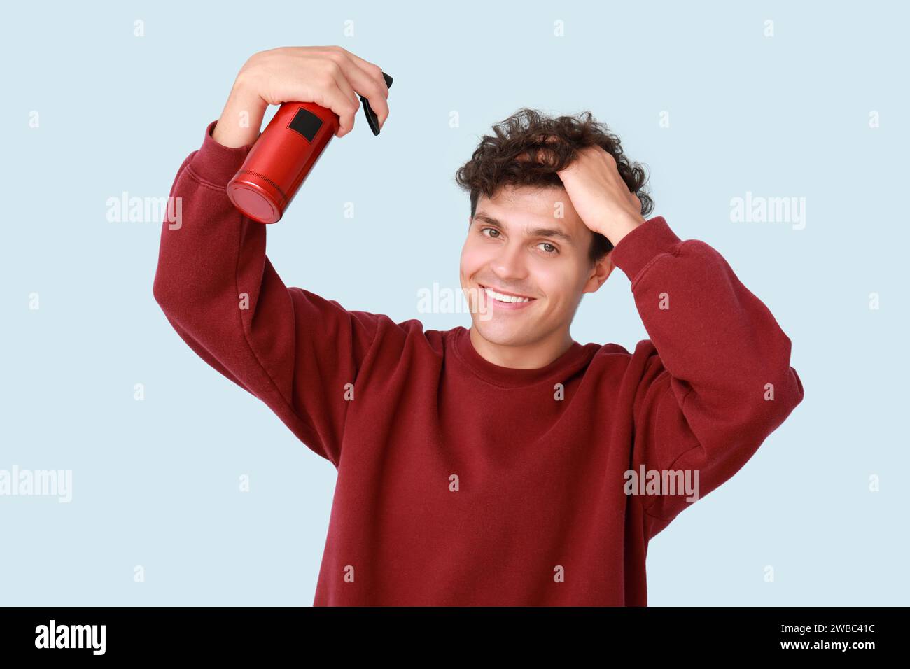 Handsome young man applying hair spray on his curly hair against blue ...