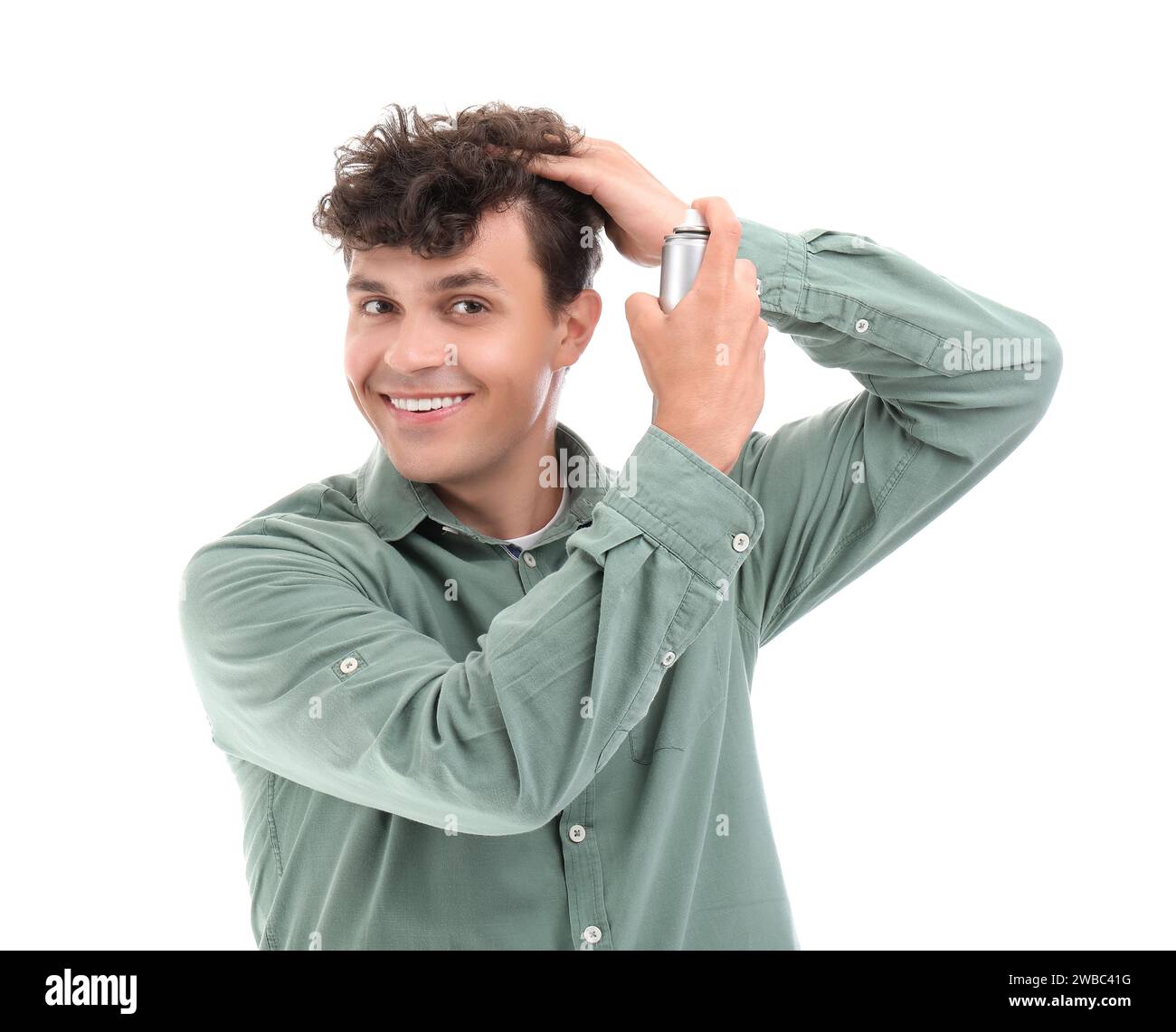 Handsome young man applying hair spray on his curly hair against white ...