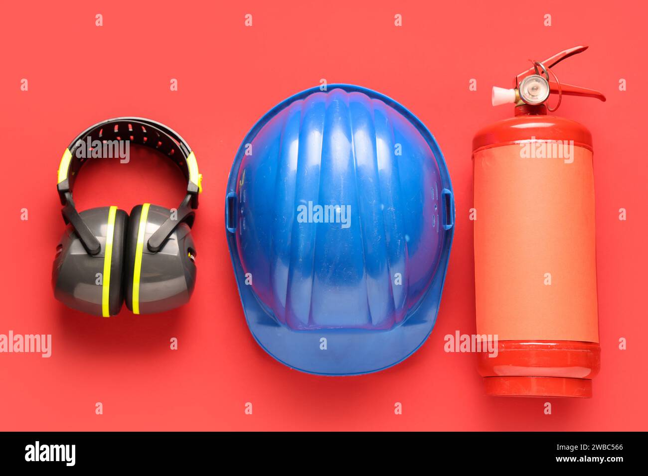 Fire extinguisher, hearing protectors and helmet on red background ...
