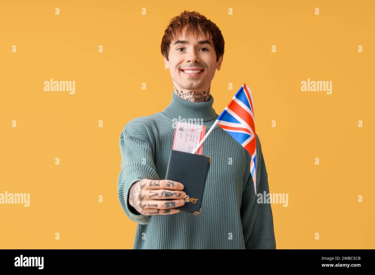 Handsome young man with UK flag and passport on yellow background ...