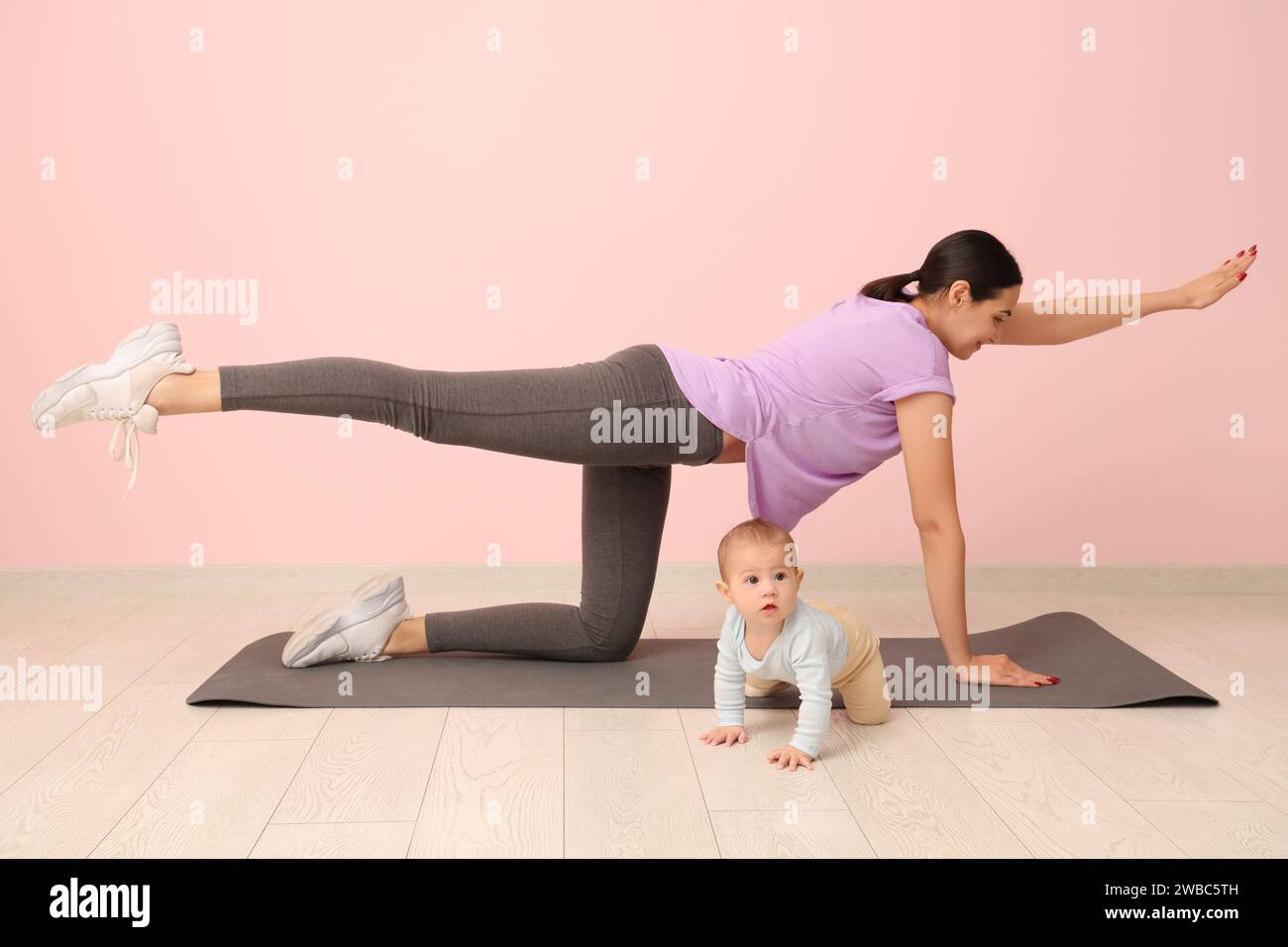 Beautiful young sporty woman with her little baby stretching near pink ...