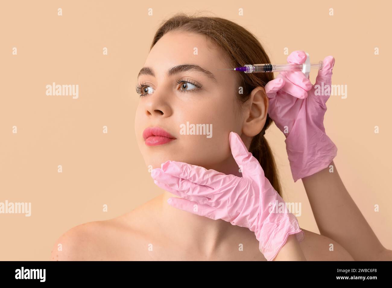 Young woman receiving filler injection in forehead on beige background ...