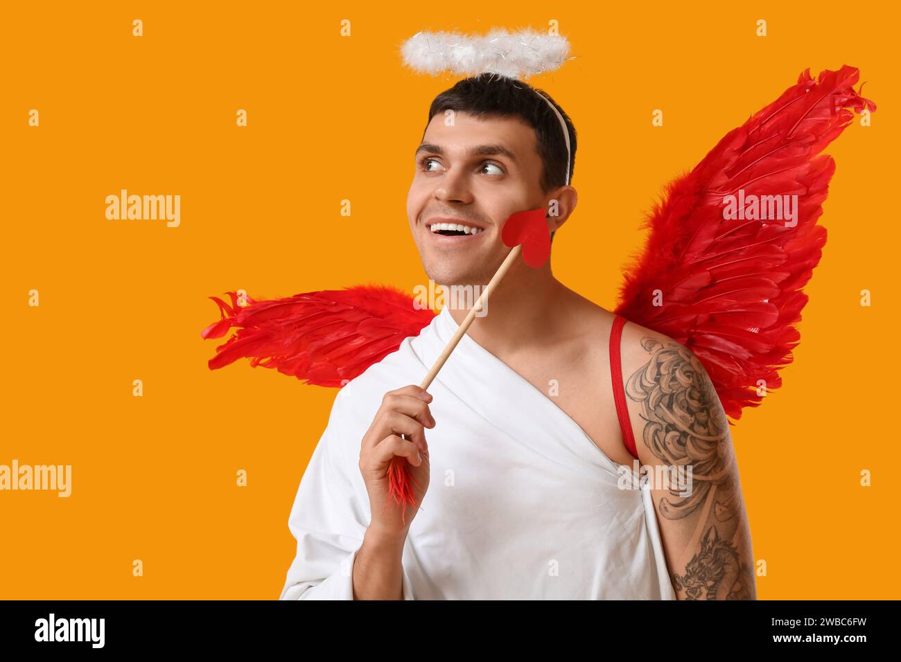 Young man dressed as Cupid with arrow on yellow background. Valentine's ...