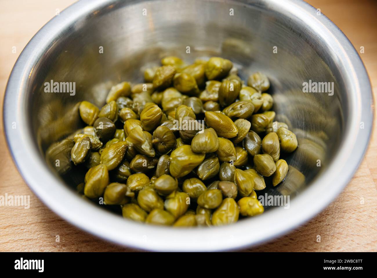Close-up view of pickled green capers in a metallic bowl, a tangy ...