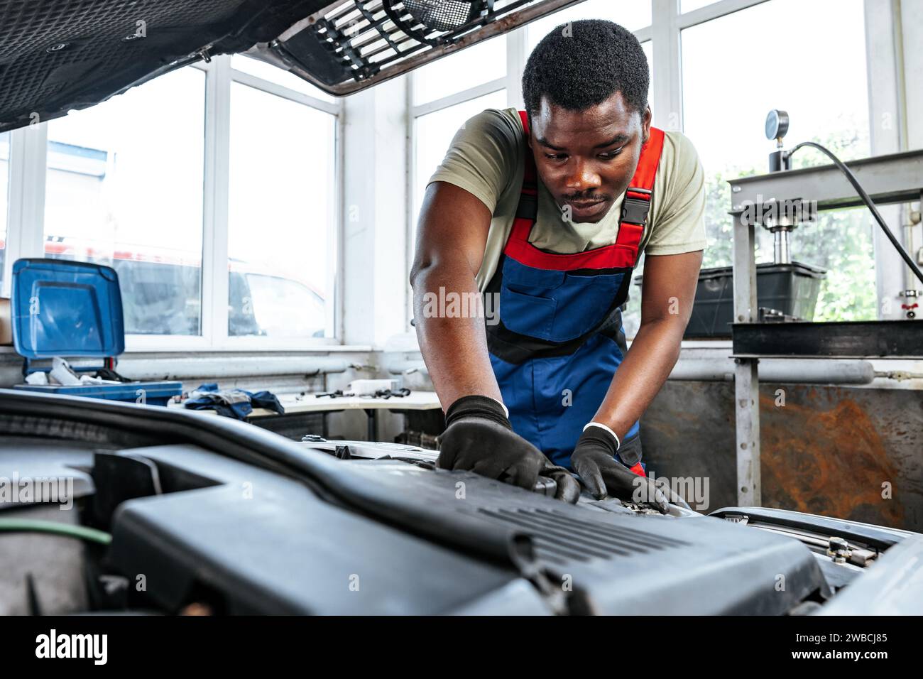 Young African man working under the hood of car fixing engine in auto ...