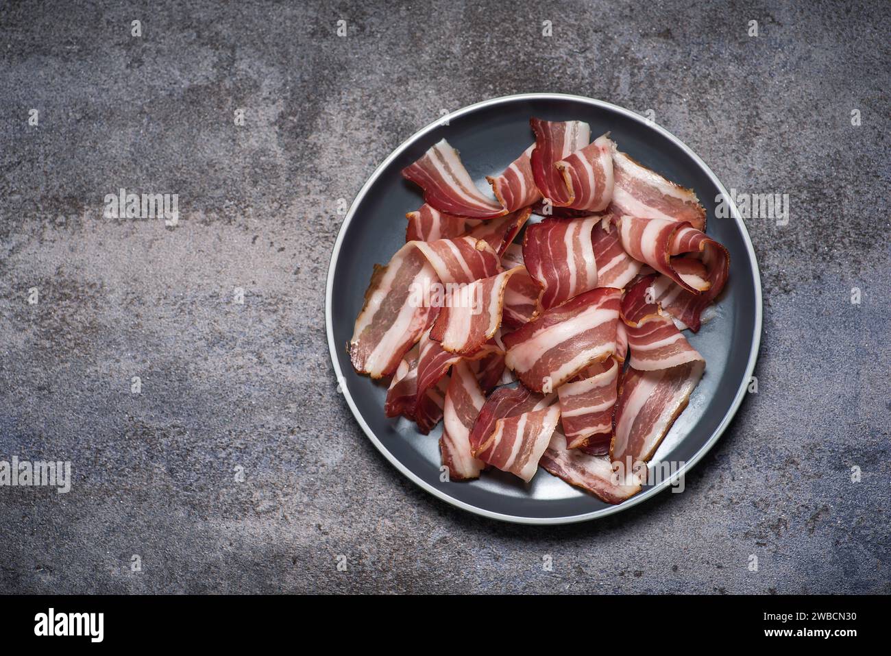 Rolled smoked bacon in a plate on a light gray background, with copy ...