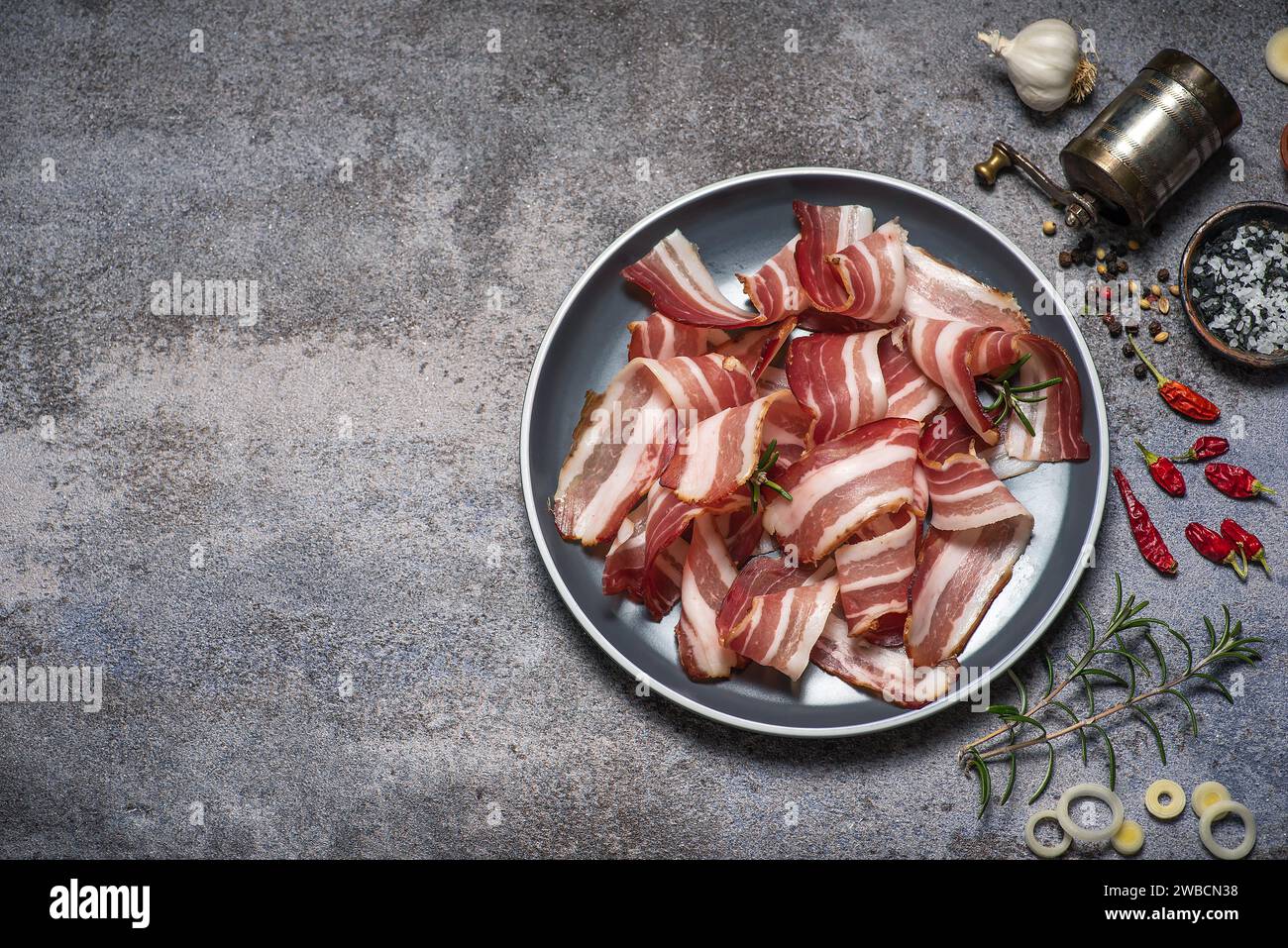 Rolled smoked bacon in a plate on a light gray background. Various ...