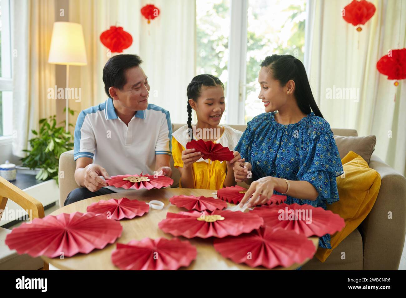 Parents and daughter making traditional red paper fans to decorate ...