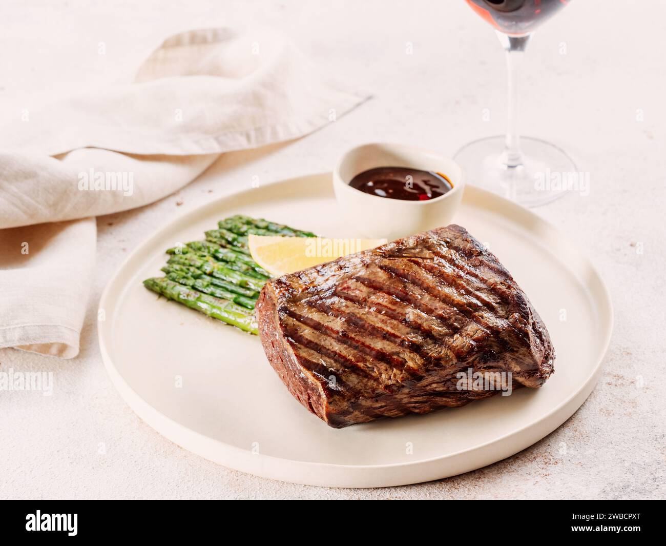 Grilled meat steak on plate with lemon and asparagus on white table ...