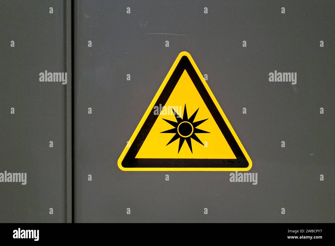 Yellow caution sign on a metal door warning about "Optical radiation ...