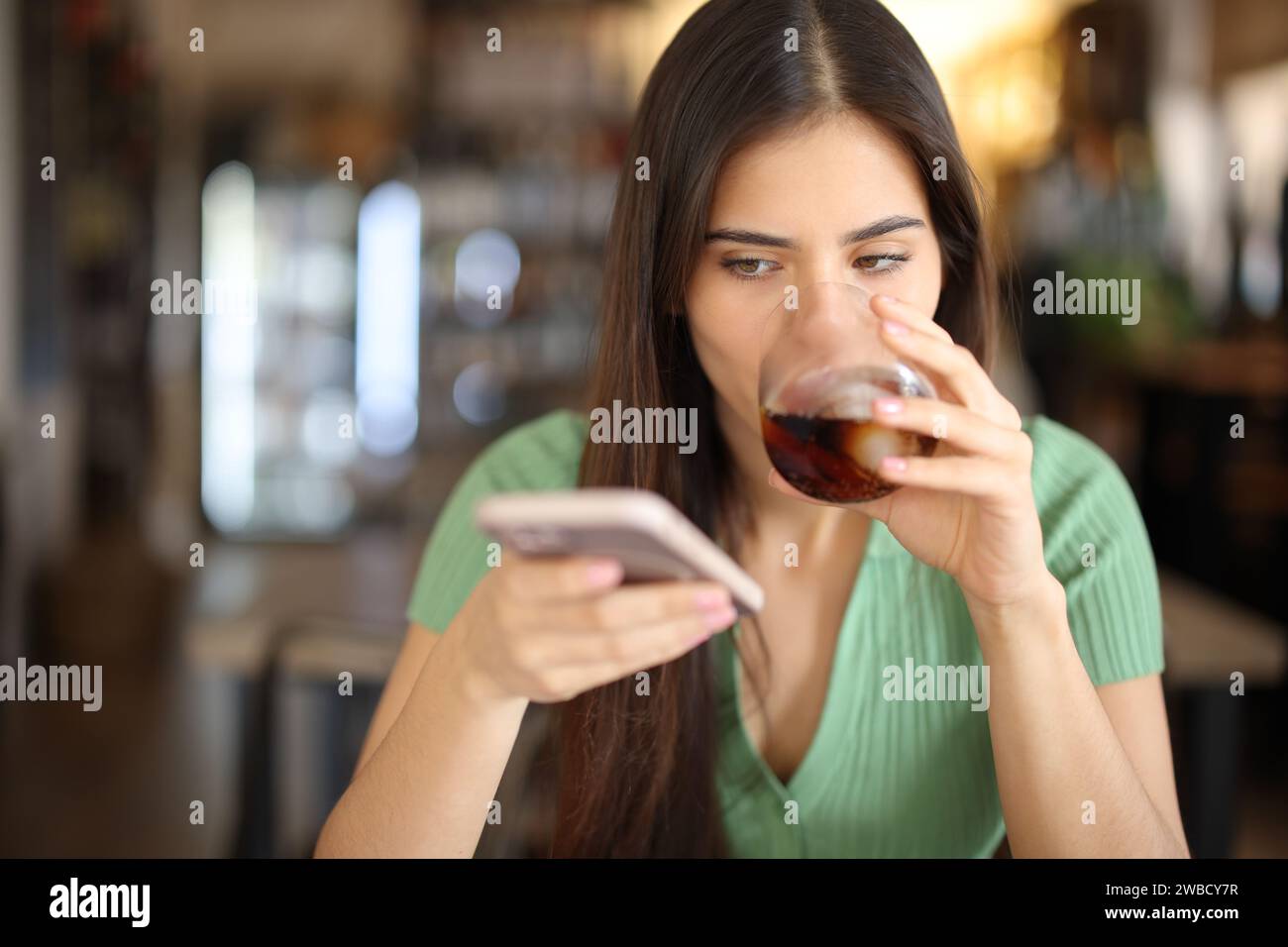 Woman in a bar checking phone and drinking soda Stock Photo - Alamy