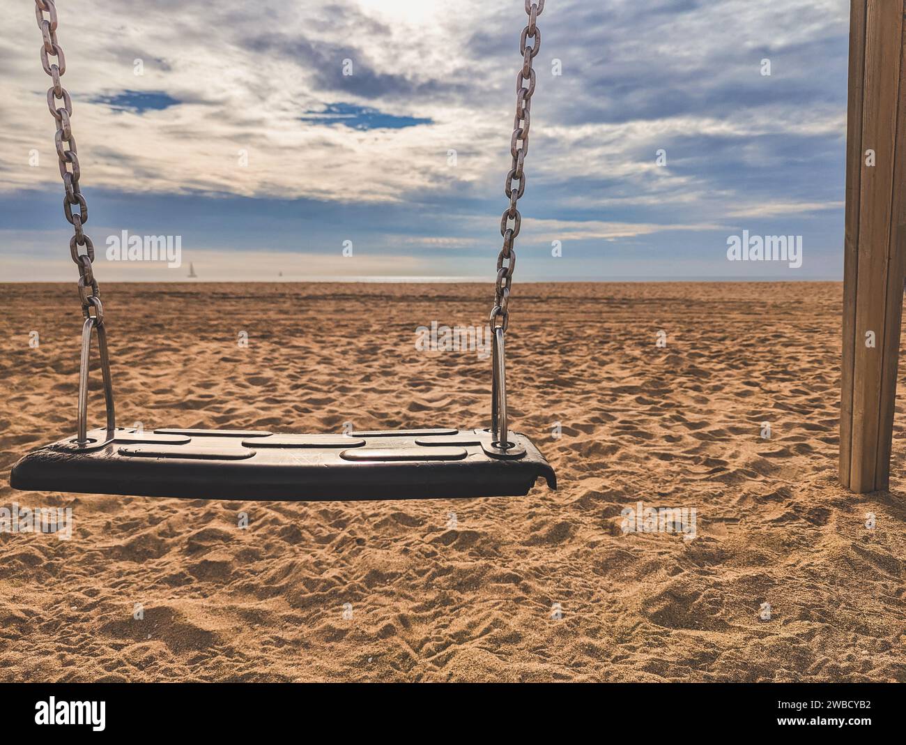 Modern black metal swing hanging on sandy ground against cloudy blue sky Stock Photo - Alamy