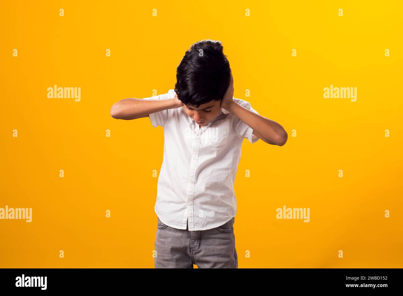 Portrait of kid boy covering ears over yellow background. Noise, stress ...