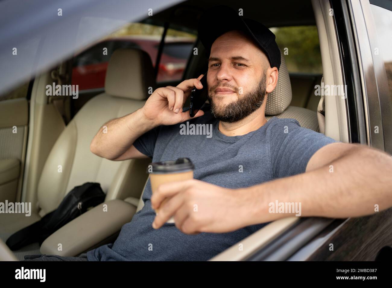 Bearded taxi driver multitasking while driving, drinking coffee and ...