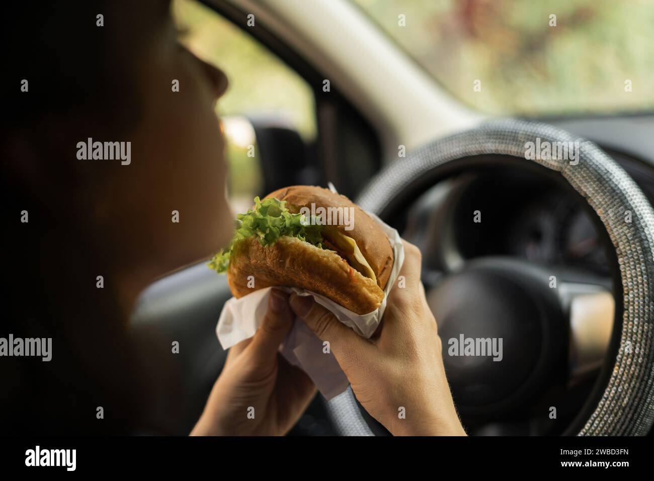 Woman eating hamburger in car in morning traffic jam on the way to work ...