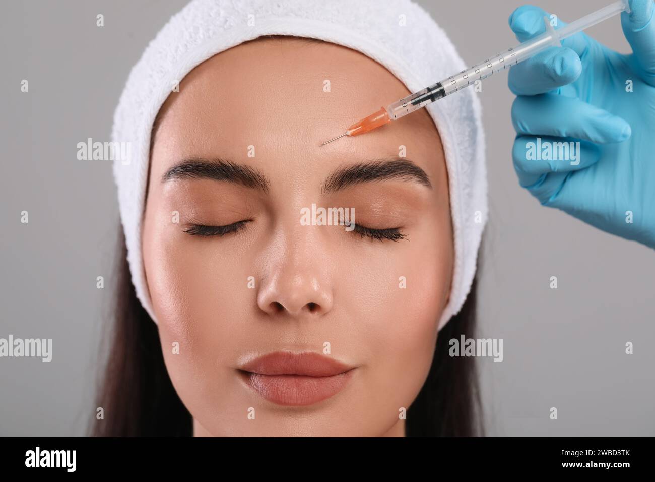Doctor giving facial injection to young woman on light grey background ...