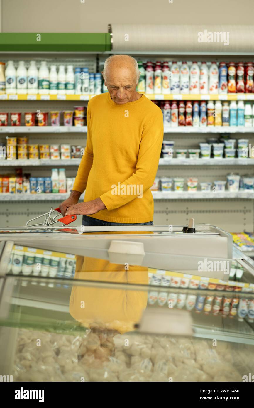 Senior man with shopping card in the frozen goods section at the ...
