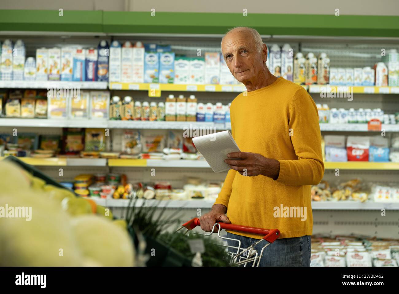 Senior customer checking her shopping list while walking with a trolley ...