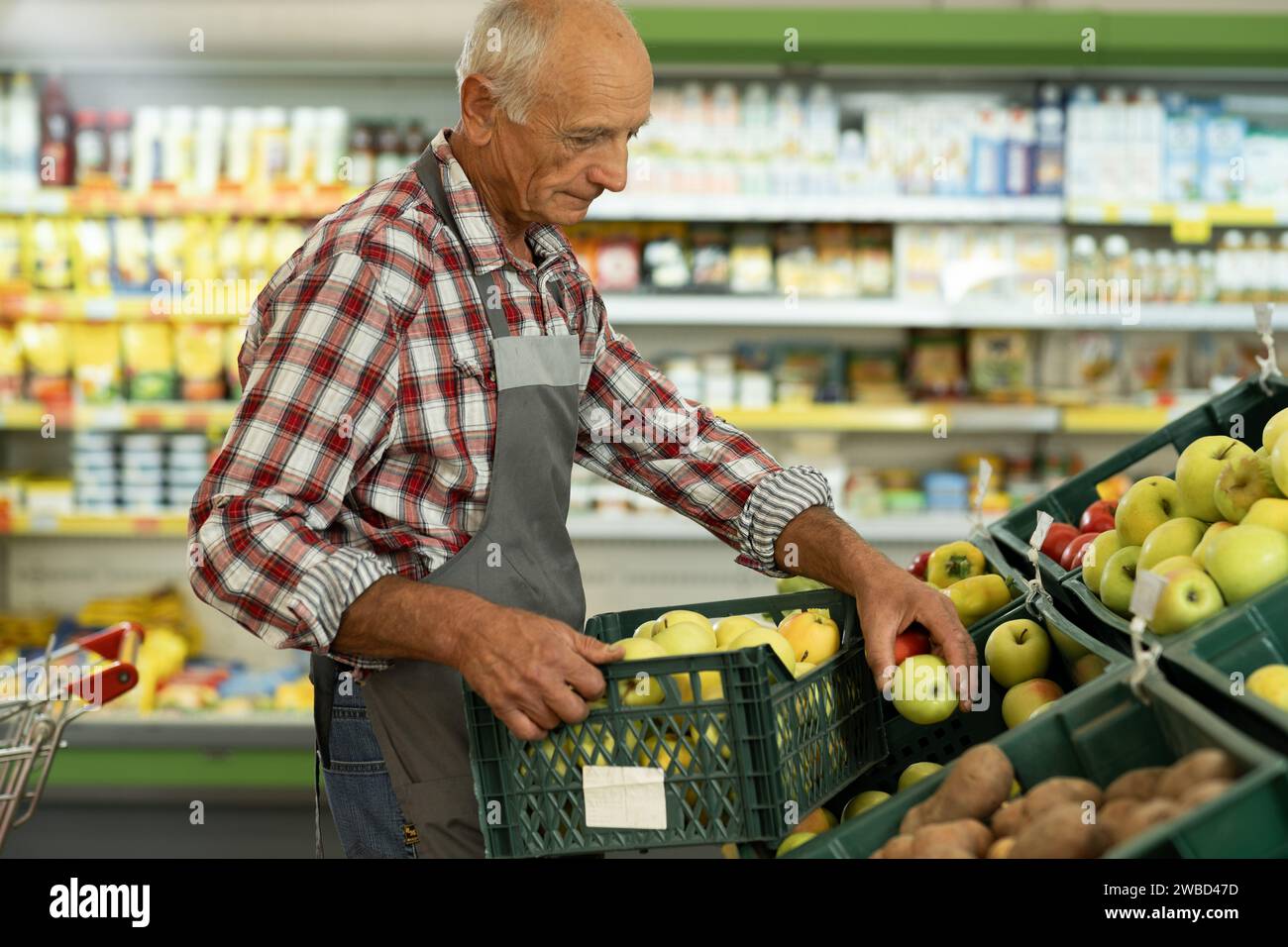 Senior man at grocery store employee, supermarket. Putting food on ...