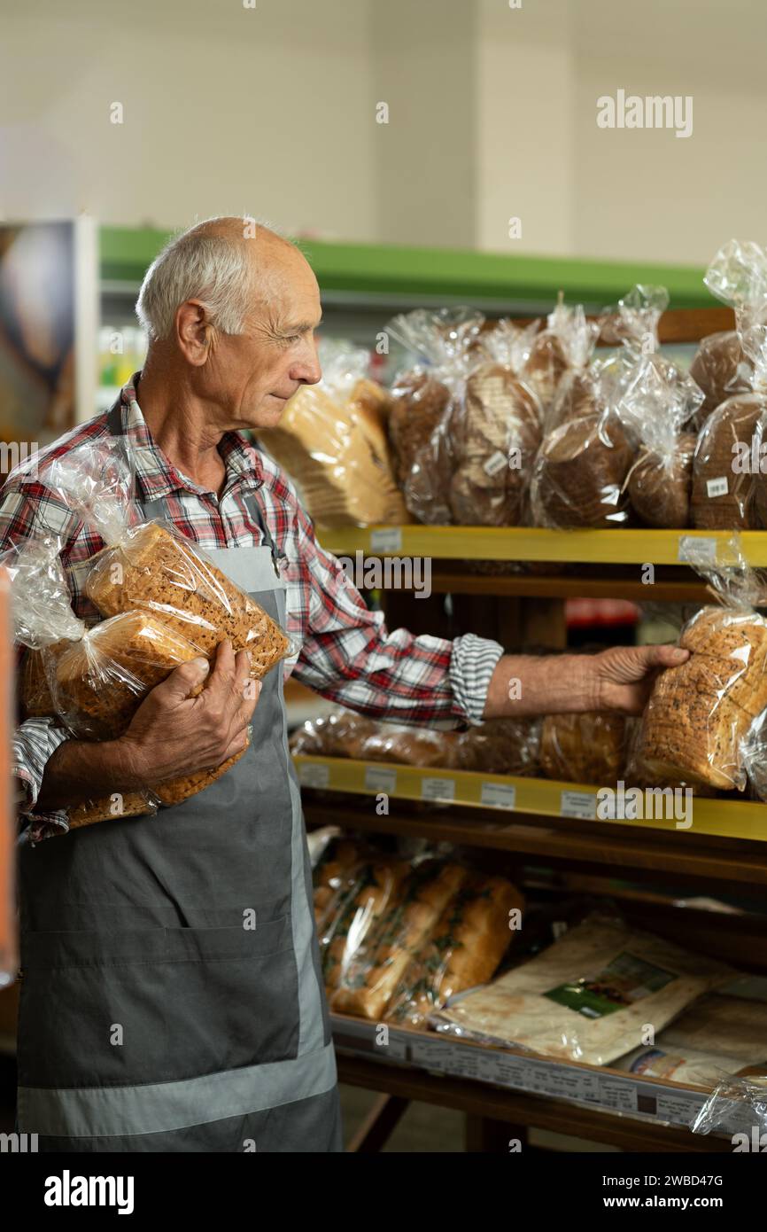 Bakery old male worker in uniform selling loaf of bread in bakehouse ...
