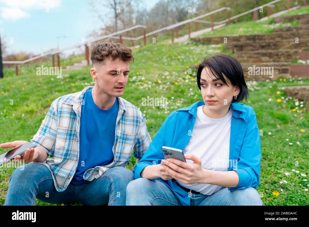 Sad couple using phones outdoors. A man peeps into a woman's phone ...