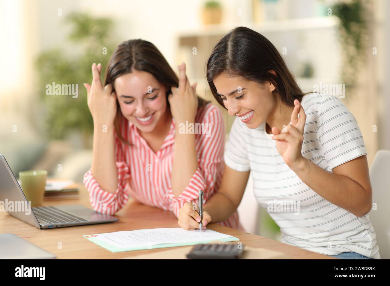 Two happy women crossing fingers signing contract at home Stock Photo ...