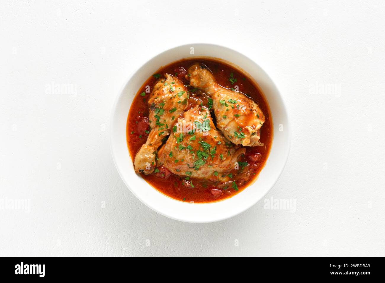 Chicken stew with tomatoes and herbs in bowl over white background ...