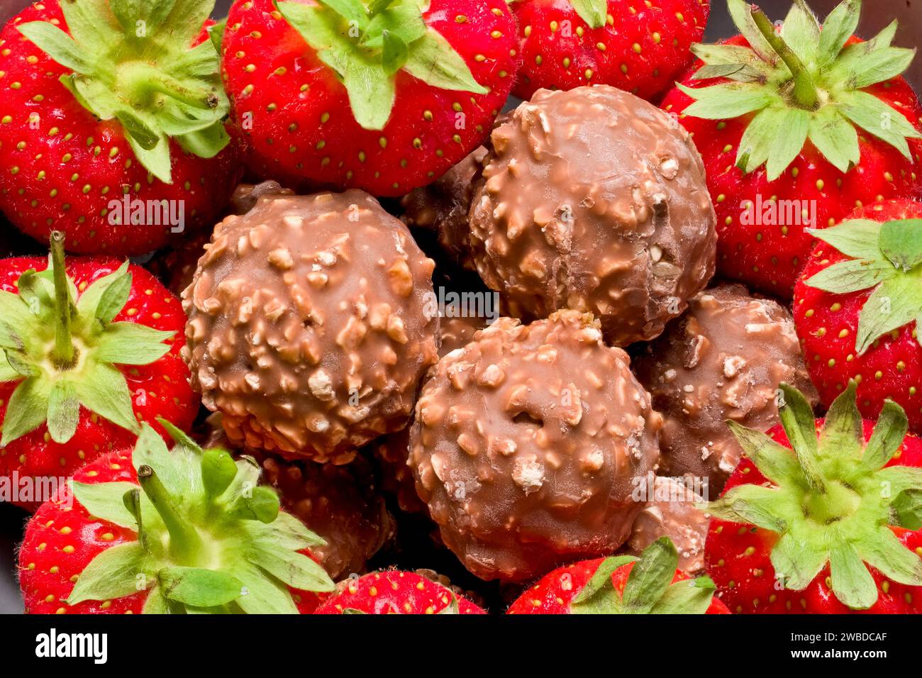 A bowl of round chocolate nut clusters with fresh strawberries ...