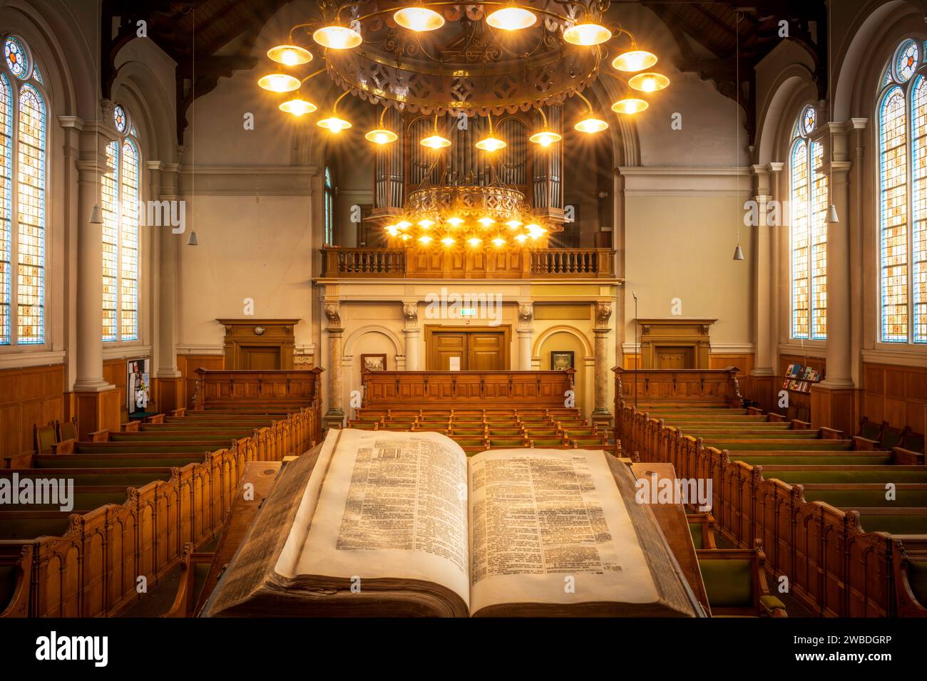 An open Bible book placed in the center of a wooden pew-filled church ...