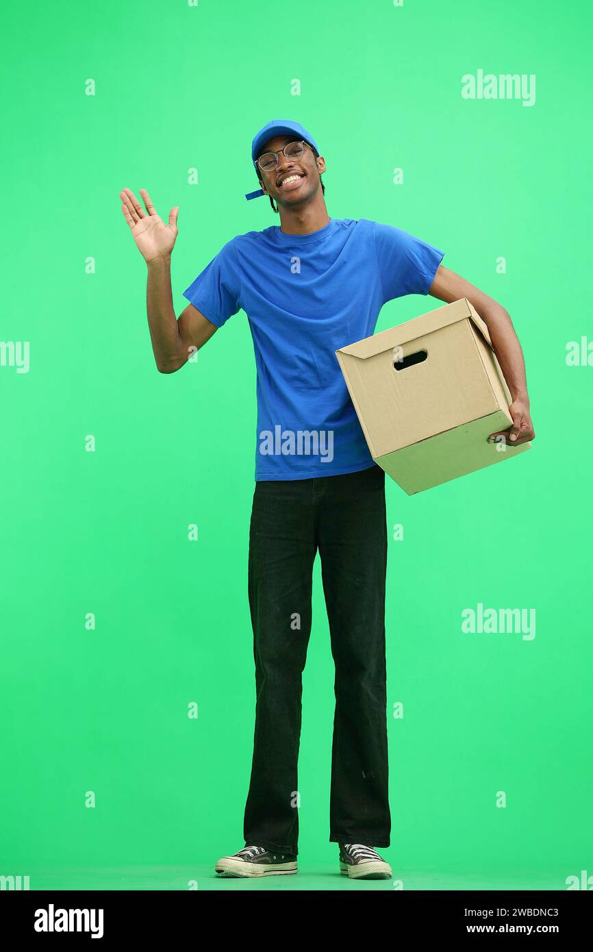 A male deliveryman, on a green background, full-length, with a box ...