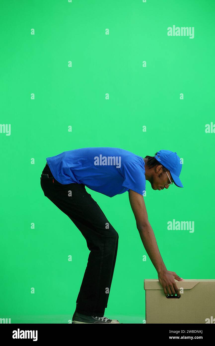 A male deliveryman, on a green background, in full height, put down a ...