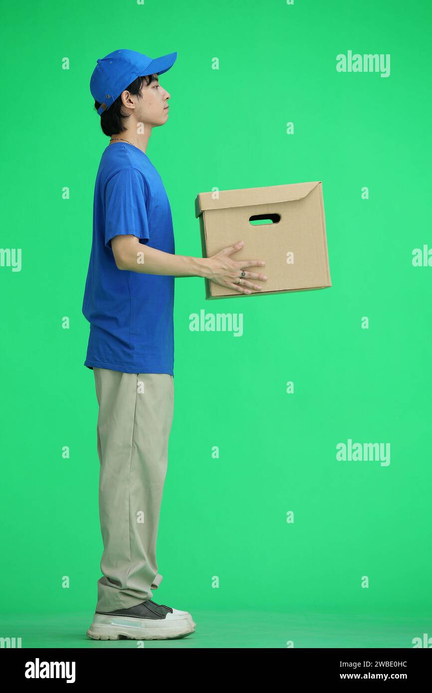 The delivery guy, on a green background, in full height, gives a box ...