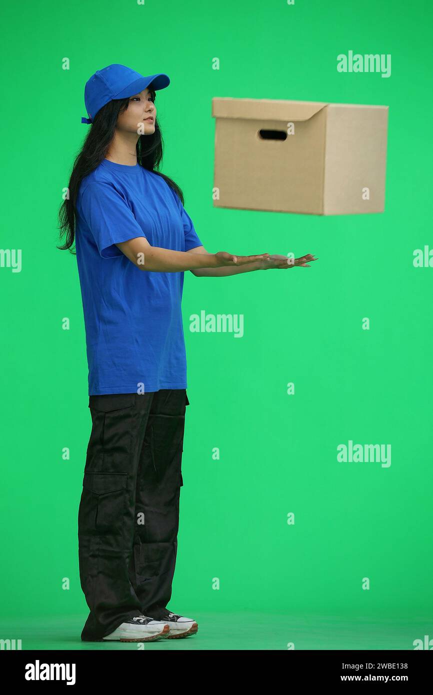 The delivery girl, on a green background, in full height, throws a box ...