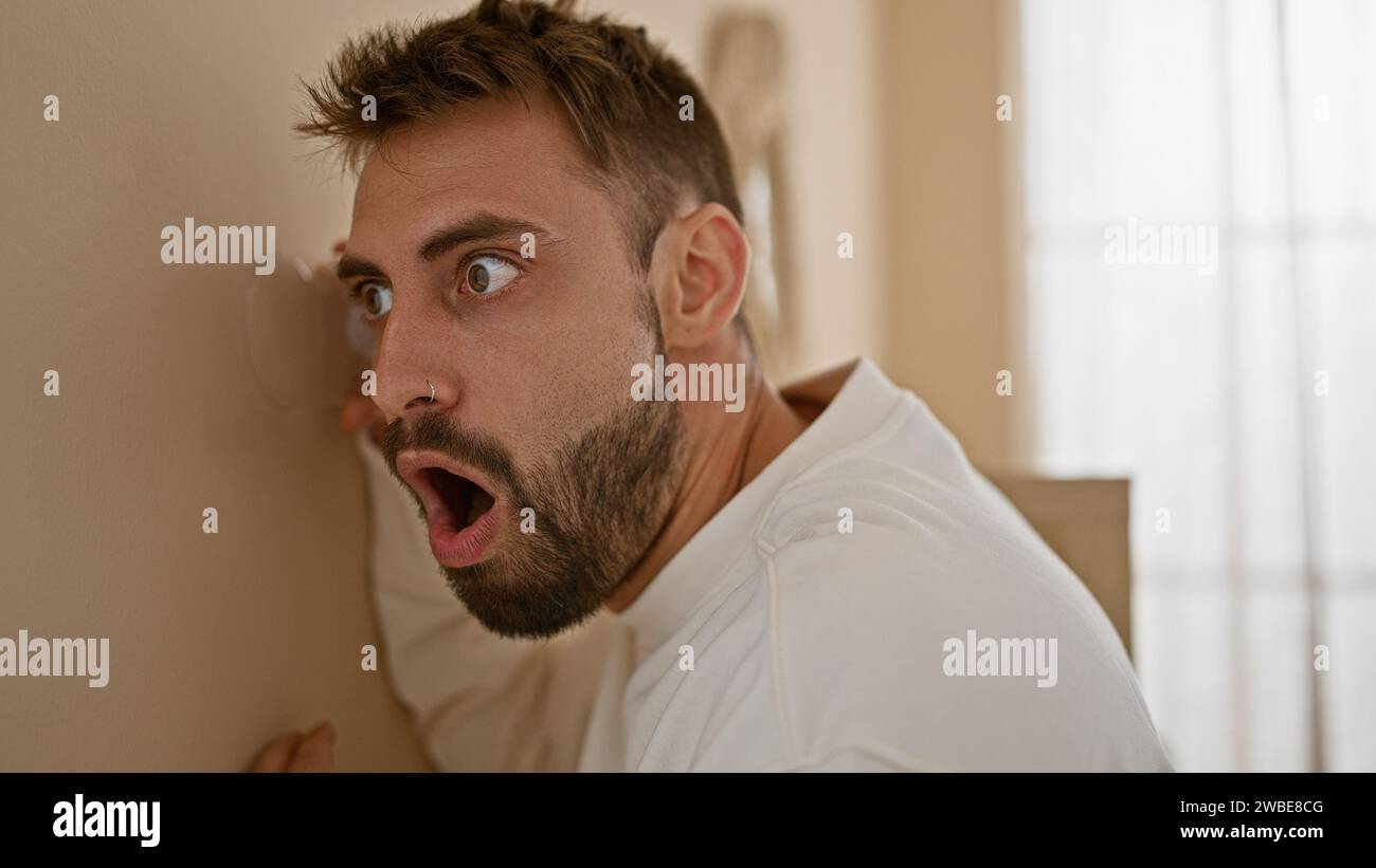 Curious young hispanic man surprised while eavesdropping through wall ...