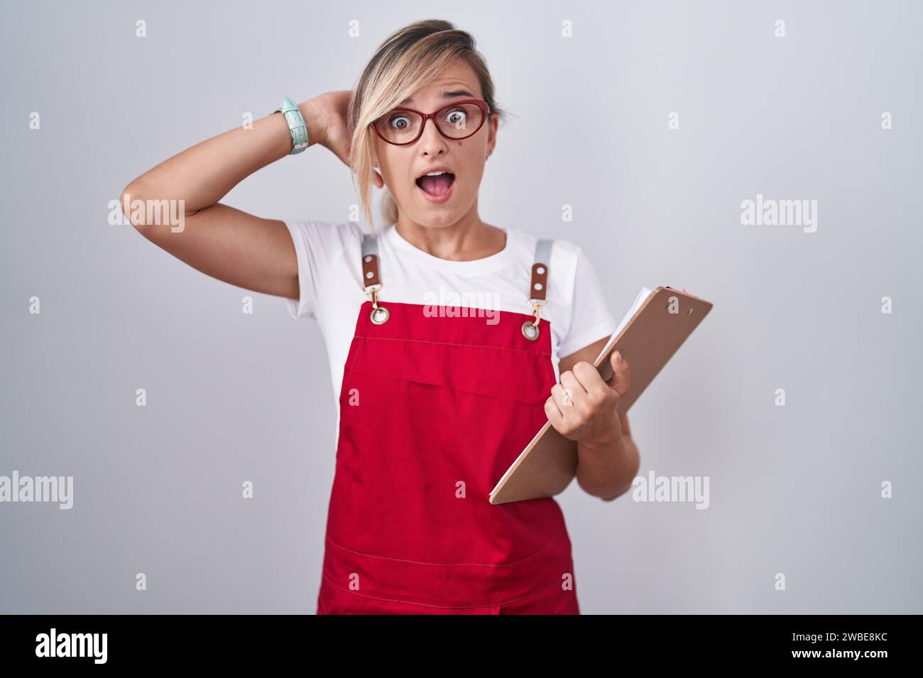 Young blonde woman wearing waiter uniform holding clipboard crazy and ...