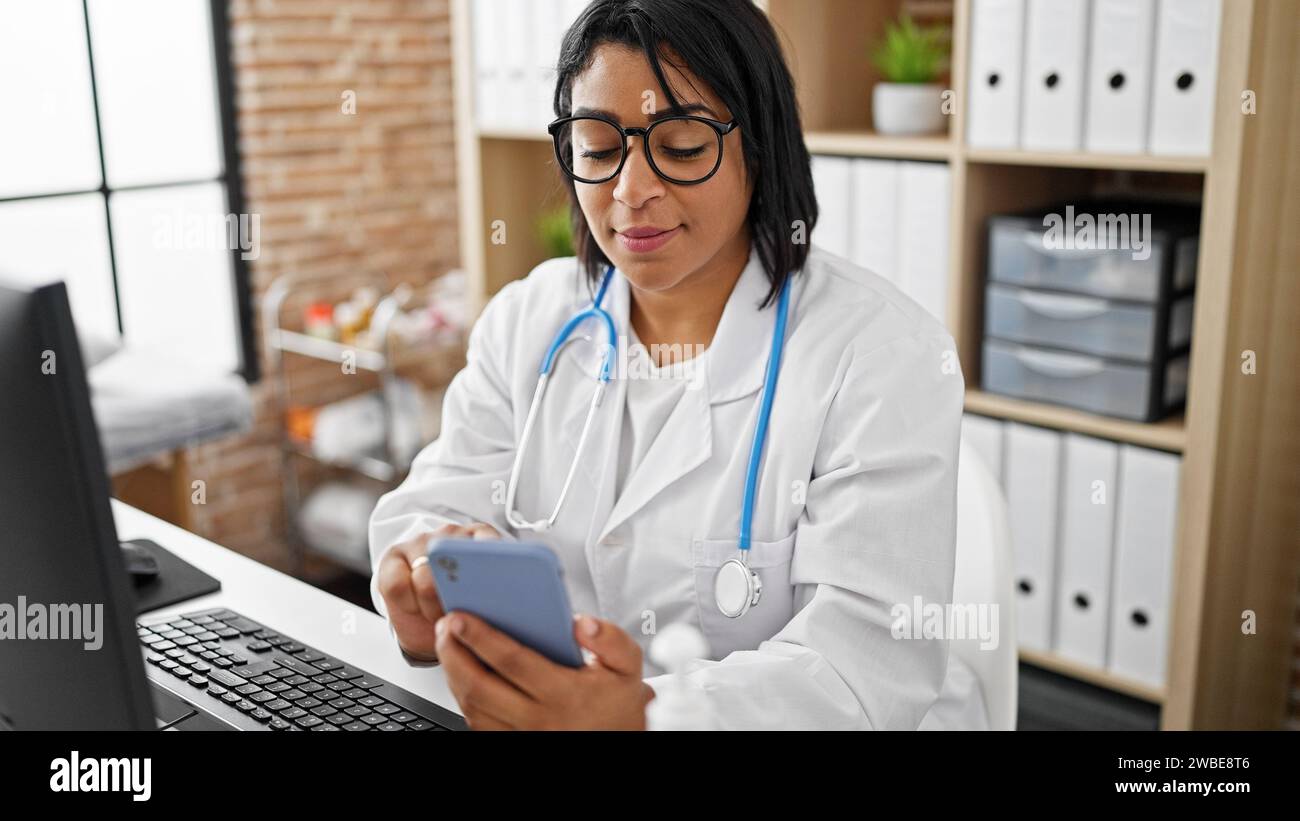 A hispanic woman doctor checks her smartphone in a well-lit hospital ...